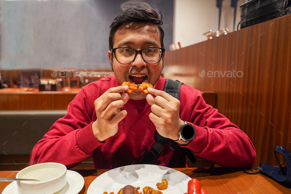 Indian man eating chicken wings at a cafe Stock Photo by wirestock