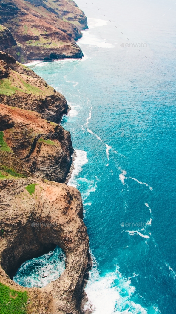 Vertical shot of the rocky cliffs by the beautiful calm blue ocean ...
