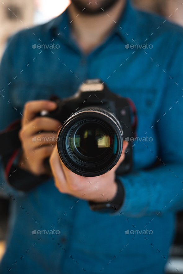 Shallow focus of a young photographer holding a modern DSRL camera ...