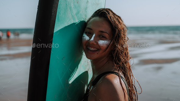 European female surfer with a sunscreen on her face holding her ...
