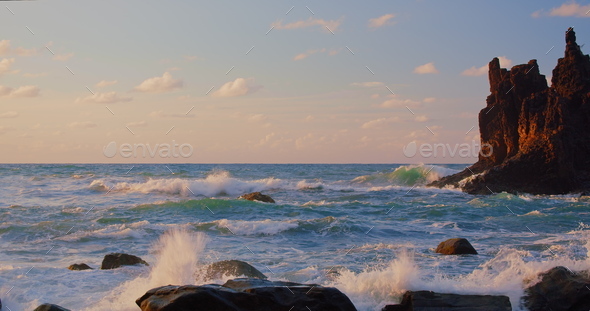 Bright sea sunset. The waves crash into the rock, lit by the warm ...