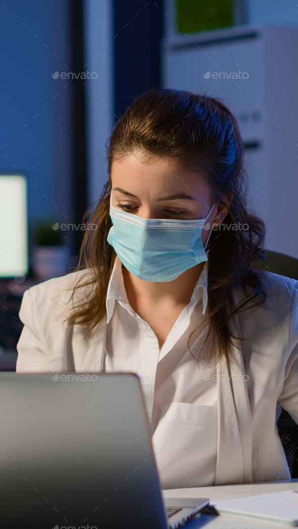 Employee with protection face mask working late at night in new normal ...