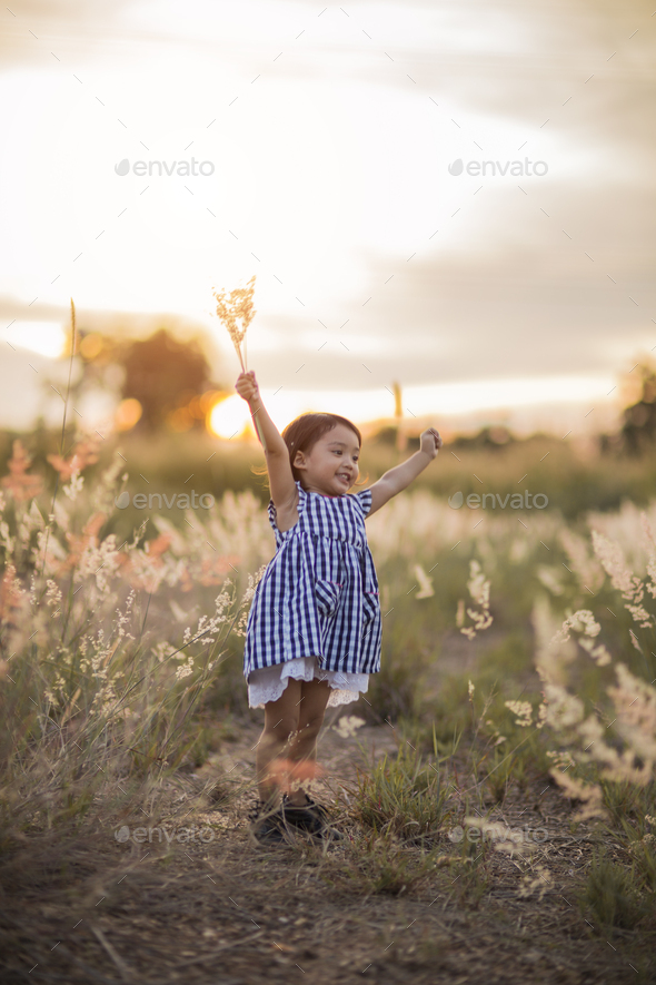 Happy cute kid in a field playing with natural spikes at summer sunset ...