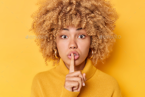 Headshot of surprised curly haired young woman presses index finger ...
