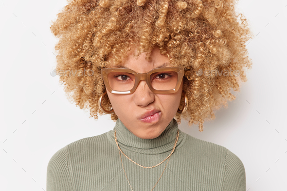 Close up portrait of angry woman with curly hair purses lips looks ...