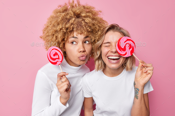 Two young women have fun pose with lollipops dressed in white clothes ...