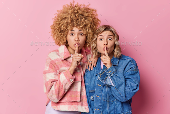 Its secret. Surprised mysterious young women make silence sign keep ...