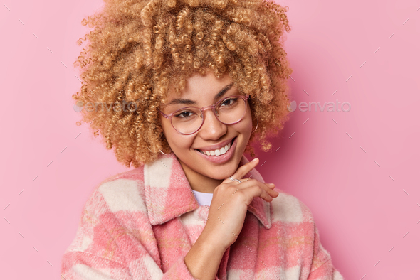 Portrait of lovely woman has natural curly hair touches jawline gently ...