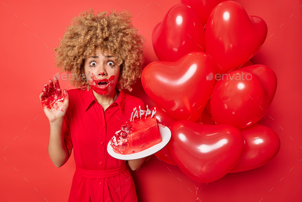 Shocked stunned woman holds cake has hand and face dirty with cream ...