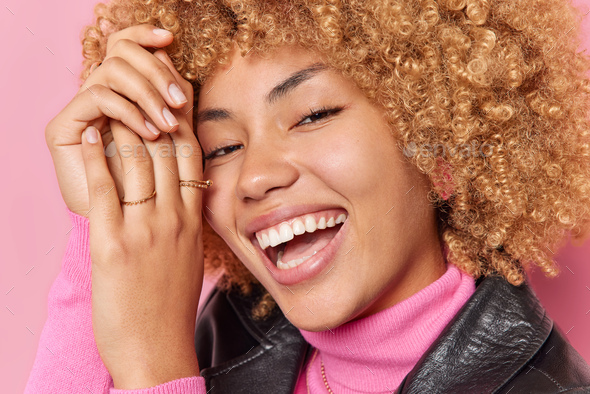 Carefree Joyful Young Curly Woman Keeps Hands Near Face Feels Very