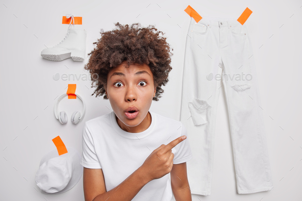 Impressed astonished curly young woman points at clothes plastered to ...