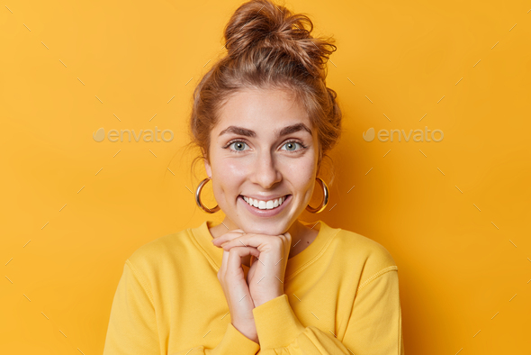 Portrait of good looking cheerful woman keeps hands under chin smiles ...