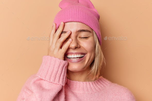 Happy woman makes face palm smiles broadly shows white teeth closes ...