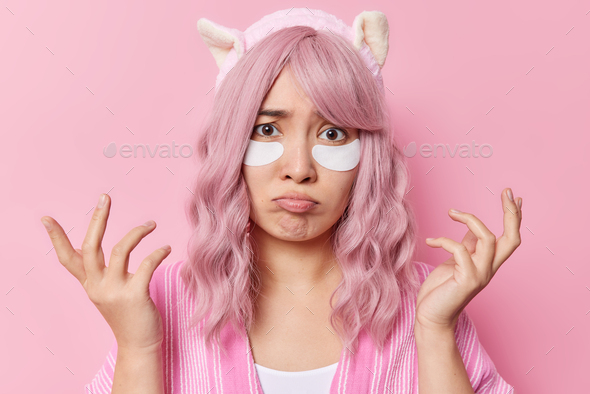 Hesitant puzzled Asian woman looks sadly keeps hands raised and looks ...