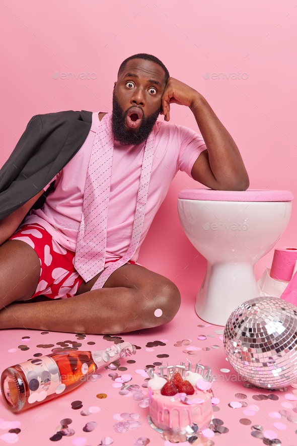 Indoor shot of shocked dark skinned man poses near toilet in restroom ...