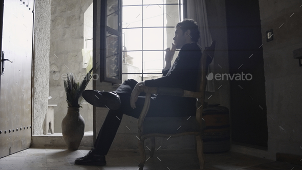 Stylish man is sitting on chair by window. Action. Elegant man in suit ...
