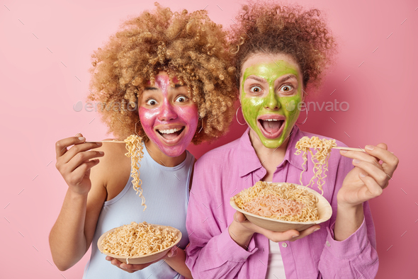 Two surprised young women with curly hair apply beauty maskon face for ...