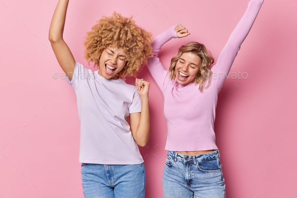 Indoor shot of overjoyed women dance carefree shake arms exclaim from ...