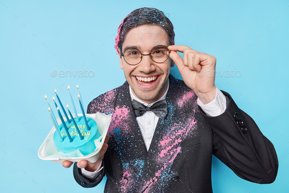Handsome man dressed in festive clothes keeps hand on rim of spectacles ...