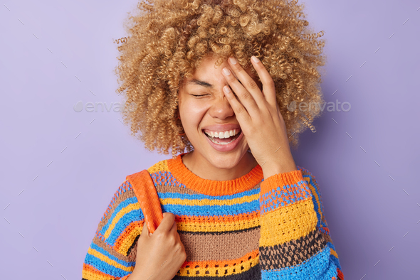 Happy curly haired woman glad expression covers half of face with palm ...