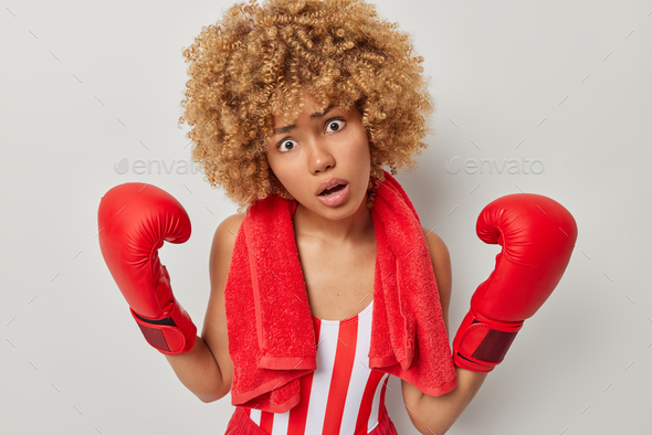 Puzzled shocked woman with curly hair makes boxing exercises wears ...