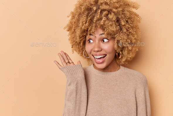 Happy surprised woman looks with great wonder aside keeps hand raised ...