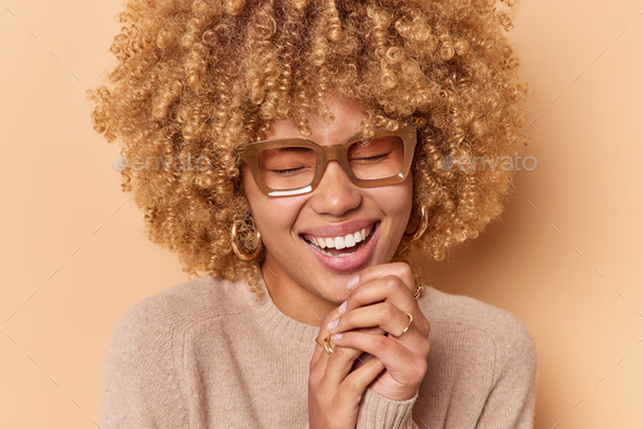 Headshot Of Overjoyed Curly Haired Woman Laughs Out Gladfully Keeps
