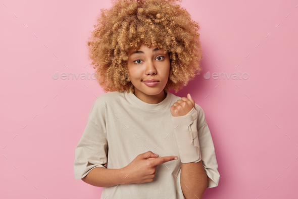 Young curly haired European woman shows broken arm after accident wears ...