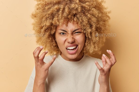 Outraged young woman with curly bushy hair gestures angrily frowns face ...