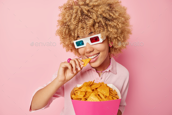 Photo of cheerful woman with curly hair eats delicious crunchy crisps ...