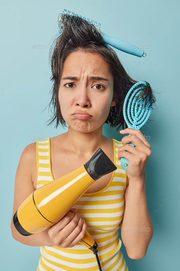 Beautiful dark haired woman uses hair dryer and comb makes hairstyle ...