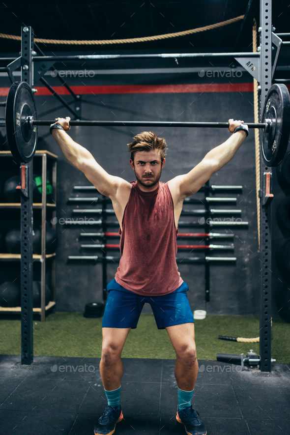 Vertical photo of a man lifting a barbell in a gym Stock Photo by riderfoot