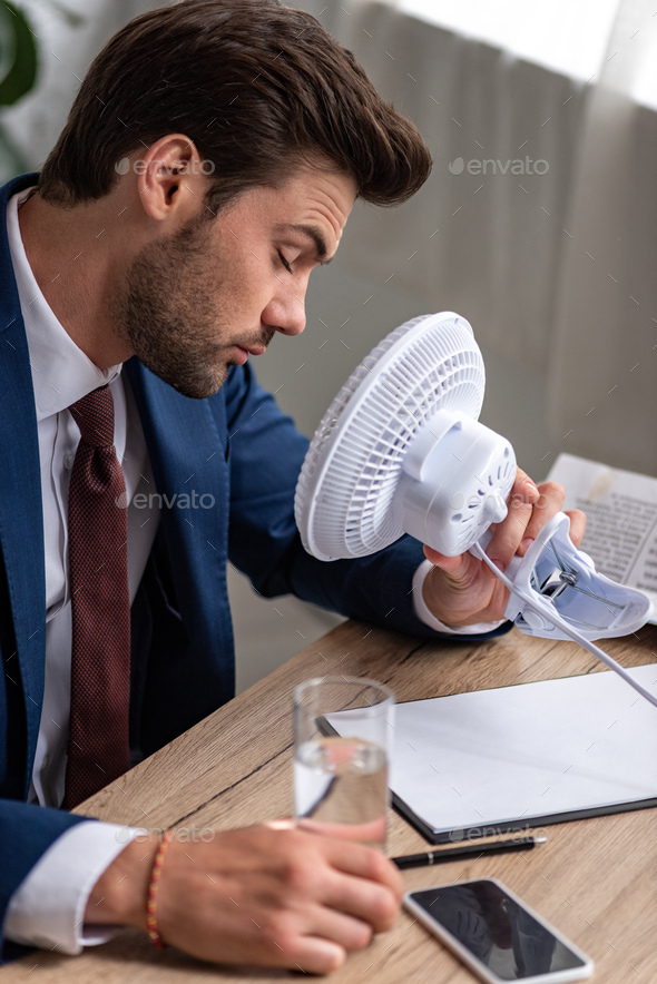 exhausted businessman sitting in front of blowing electric fan while ...