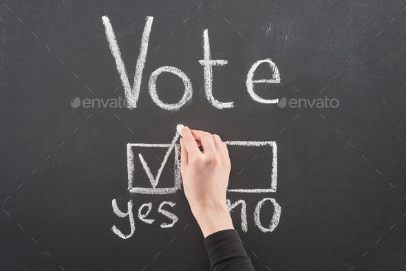 top view of voter putting check mark near yes word on black chalkboard ...