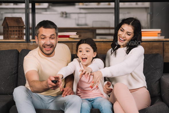 happy man holding remote controller near daughter and wife at home ...