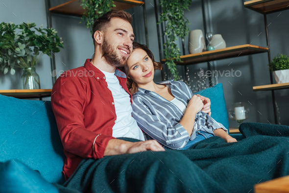 happy man hugging attractive woman while sitting on sofa at home Stock ...
