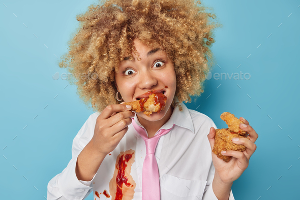 Positive surprised curly haired woman eats delicious nuggets with ...