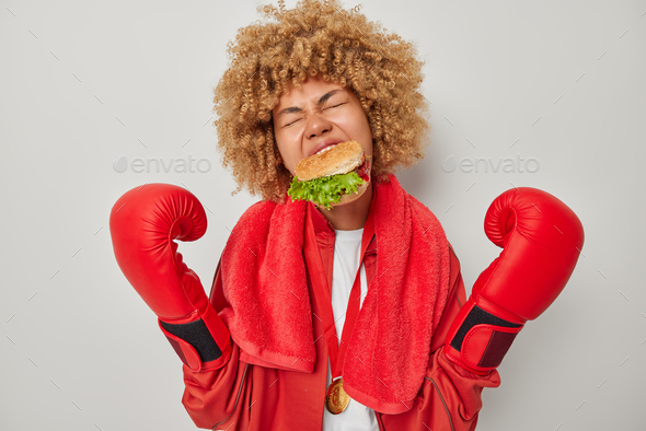 Depressed curly haired female boxer bites delicious sandwich breaks ...