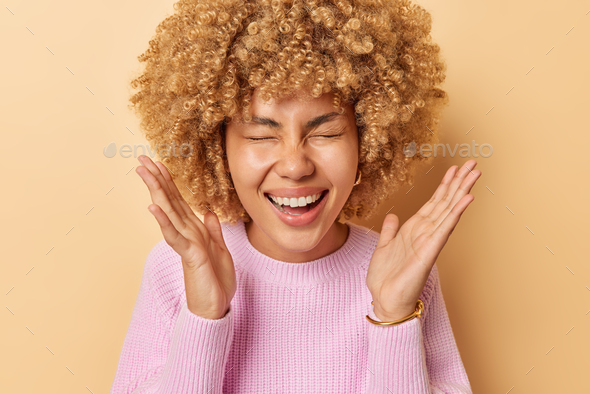 Overjoyed Curly Haired Woman Keeps Palms Raised Laughs Joyfully Smiles