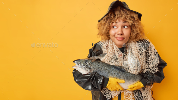 Happy thoughtful woman holds big caught fish returns after fishing with ...