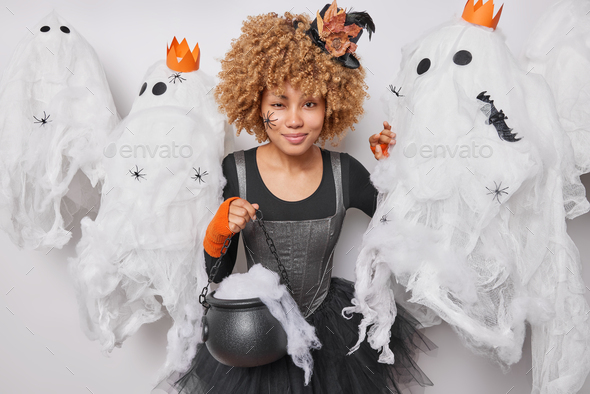Pretty pleased curly haired female witch poses with cauldron involved ...