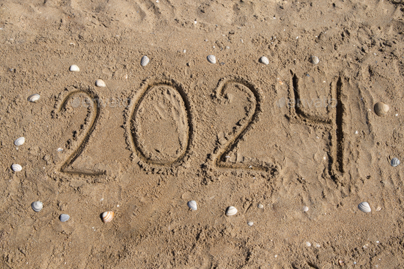 The numbers 2024 are handwritten on the sand, on the seashore, seashell ...
