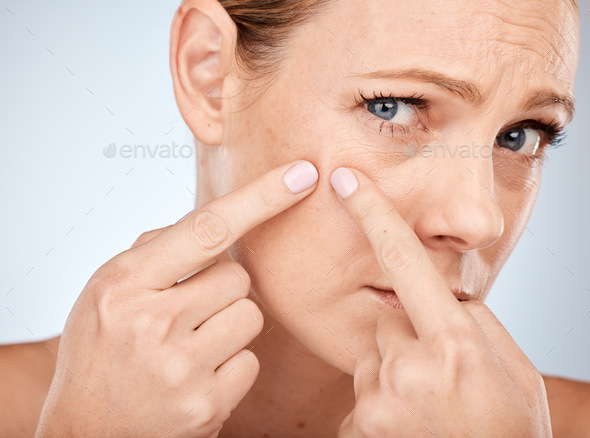 Health, skincare and woman popping acne in face with studio background ...