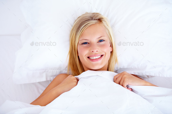 Waking up well-rested. Gorgeous young woman lying in bed smiling up at ...