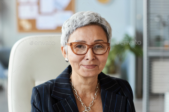 Senior woman as female boss sitting at workplace and smiling at camera ...