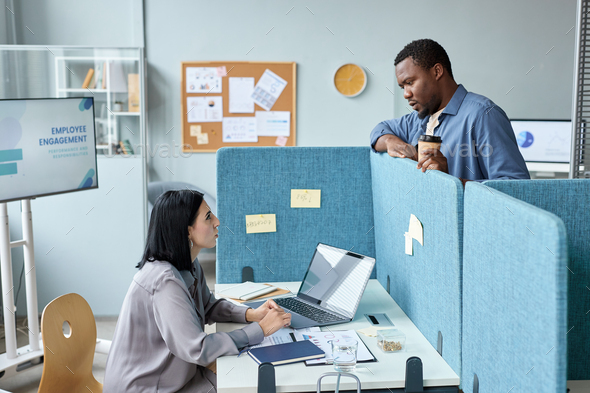 Two young colleagues talking over cubicle wall in office Stock Photo by seventyfourimages