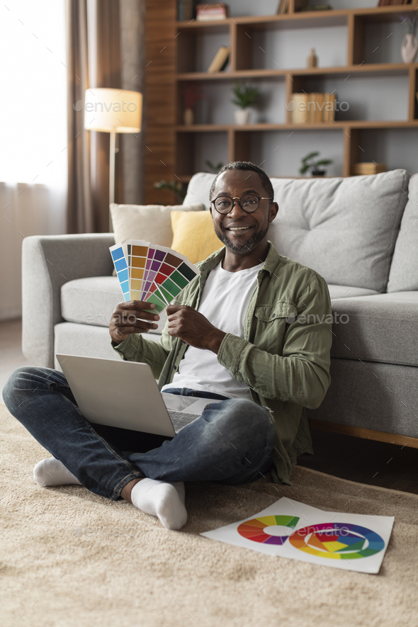 Cheerful adult black man in glasses uses computer, works with color ...