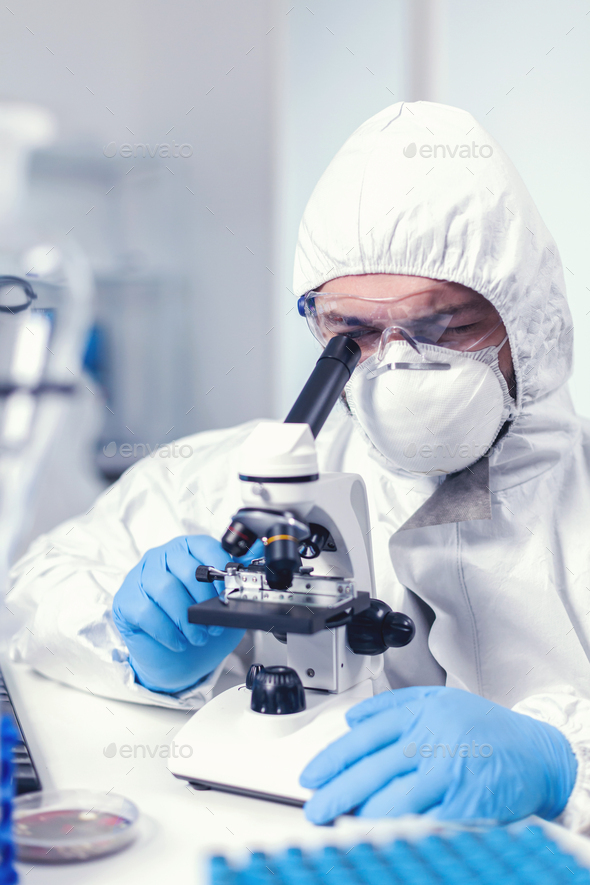 Medical engineer adjusting microscope wearing ppe Stock Photo by DC_Studio