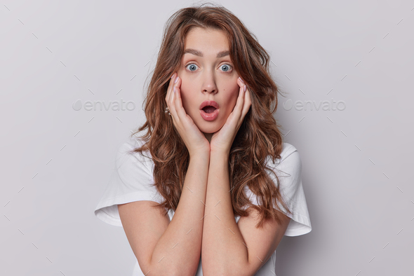 Horizontal shot of stupefied woman with dark wavy hair keeps hands on ...