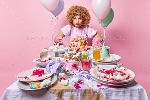 Unhappy gloomy young woman poses near messy table after birthday party ...